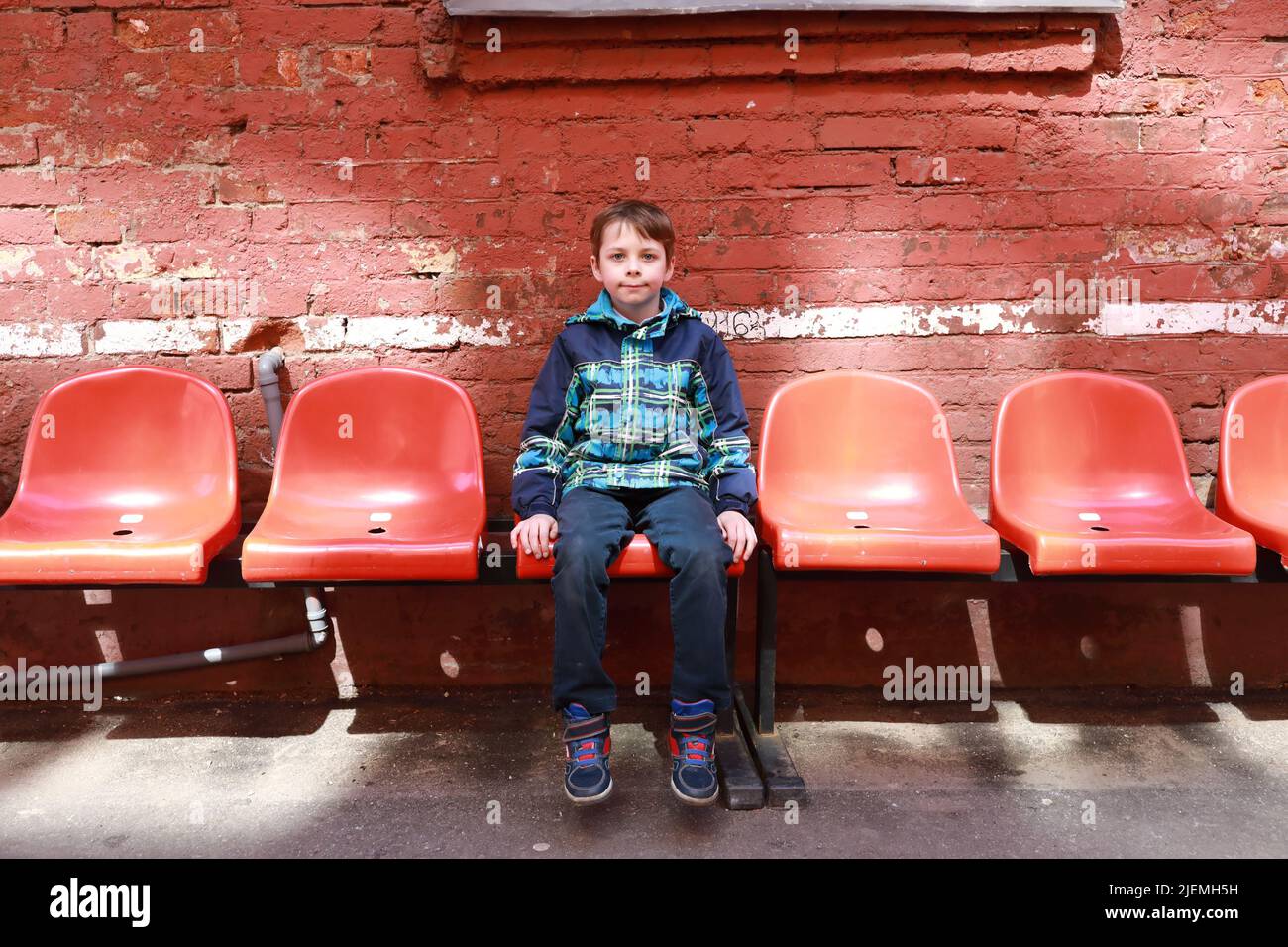 Child sitting on red chair against brick wall Stock Photo - Alamy