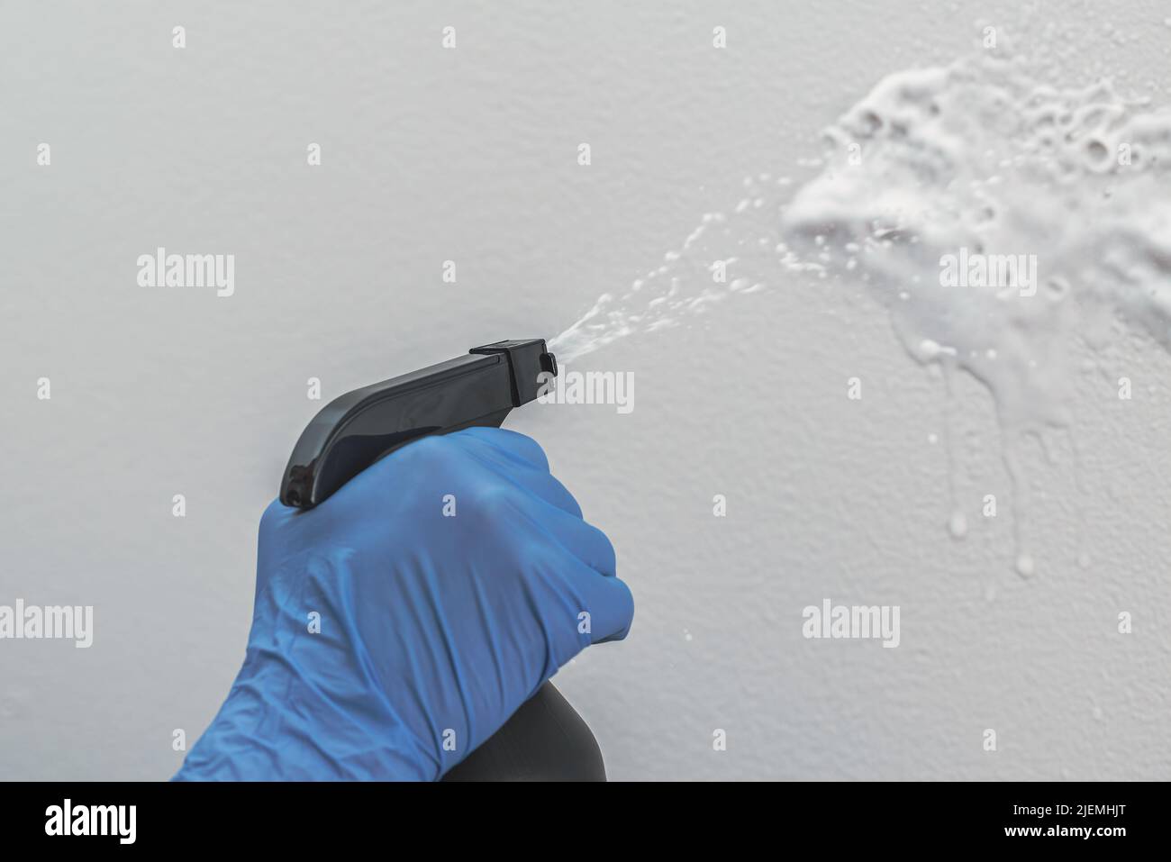 Cleaning concept. Woman hand in blue gloves cleaning white wall with ...