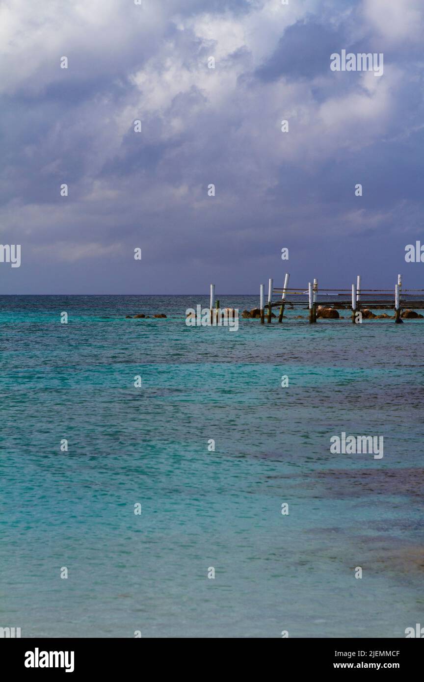 An old pier falling apart in tropical waters, with a cloudy sky and ...
