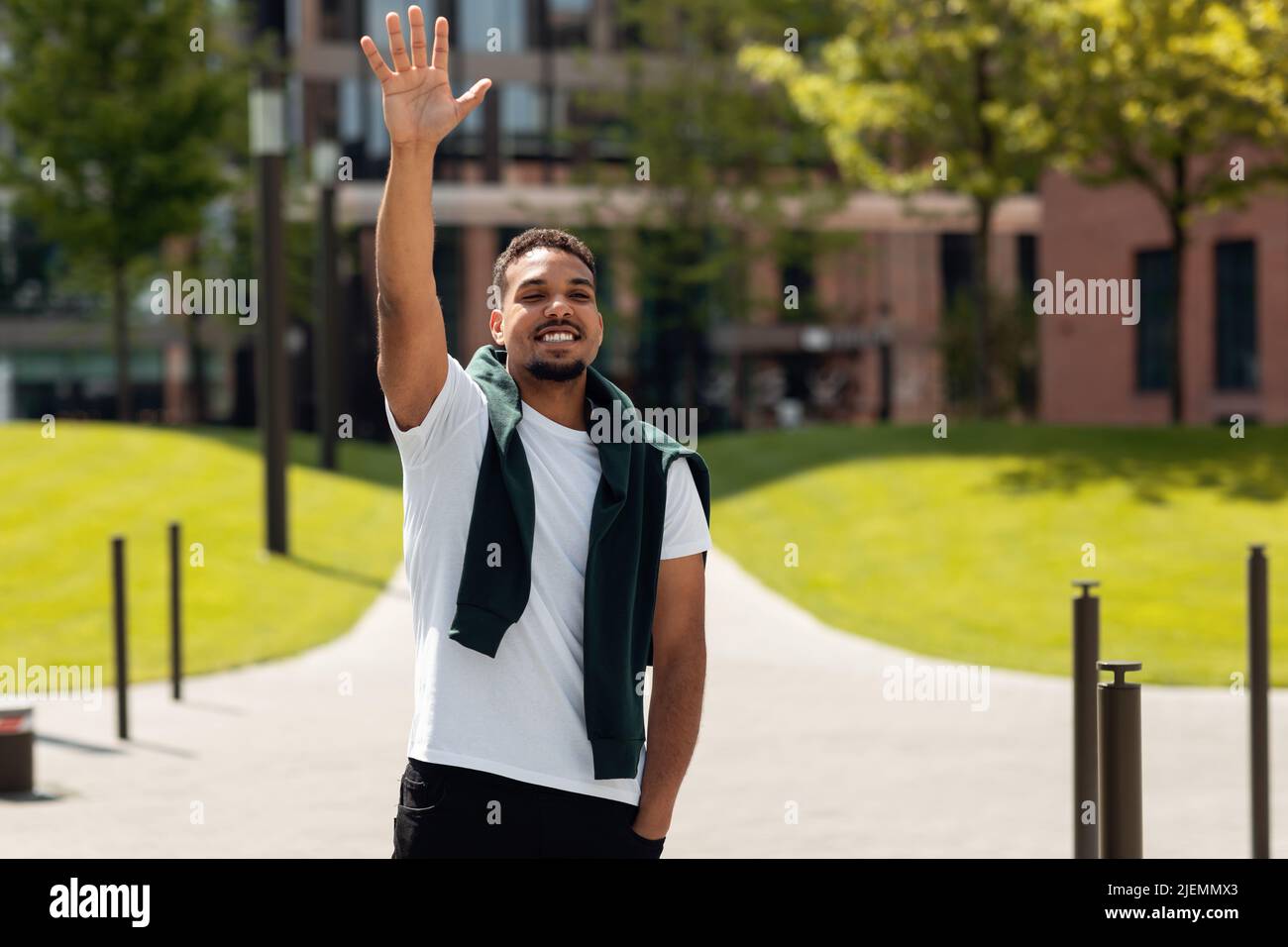Happy african american guy waving hand and greeting friends outdoors ...