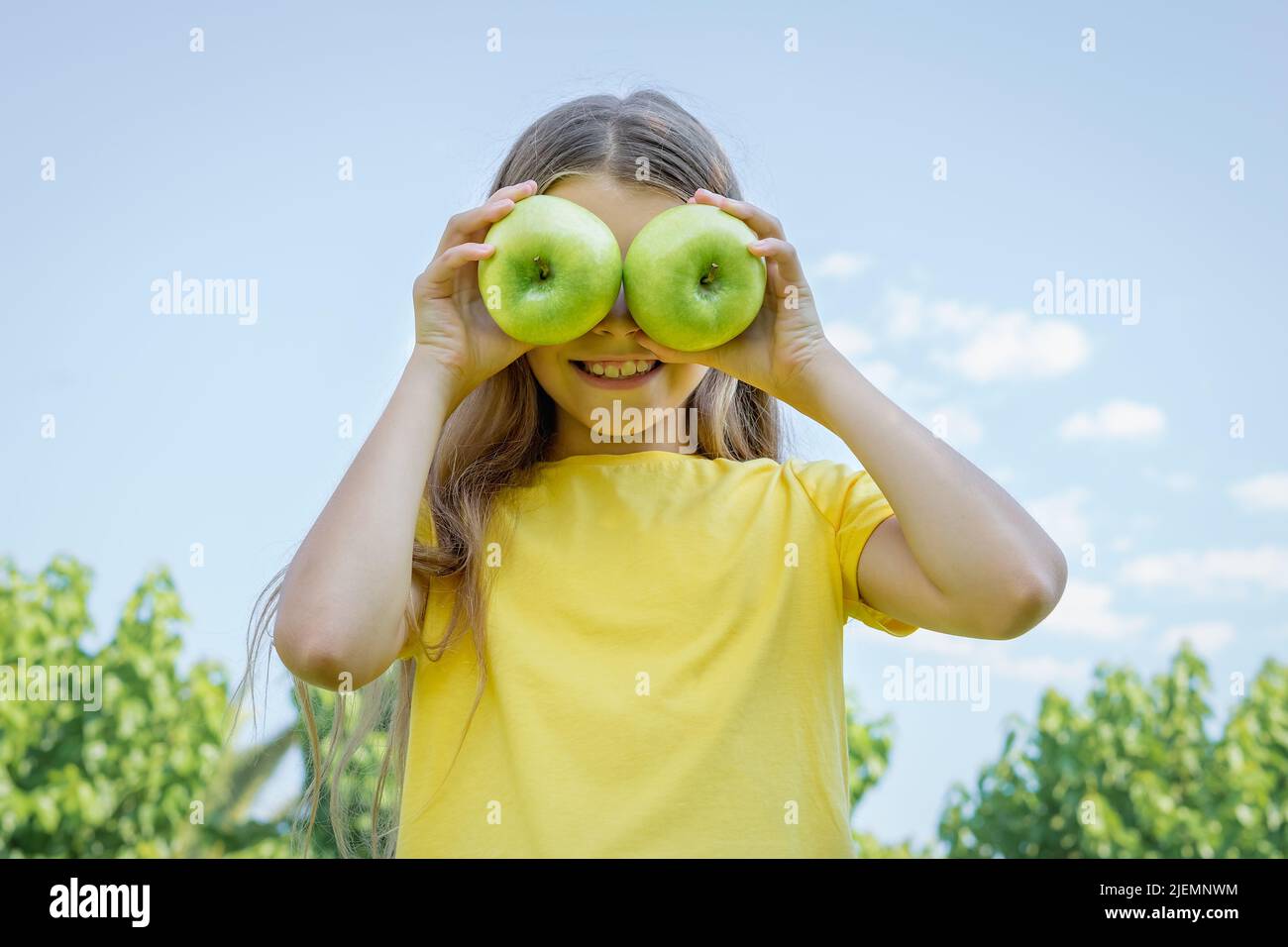 A teenage girl holds two apples in front of her face in the park Stock ...