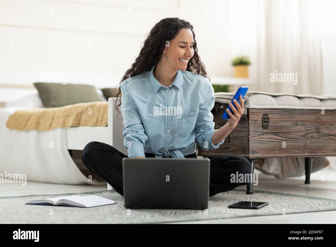 Focused young lady using laptop and smartphone for online work or ...
