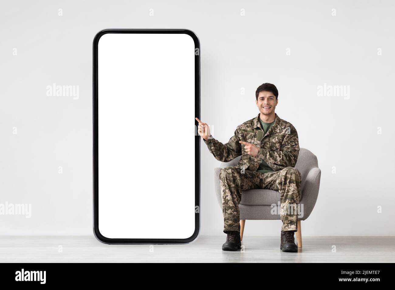 Smiling soldier in military uniform sitting by huge phone, mockup Stock ...