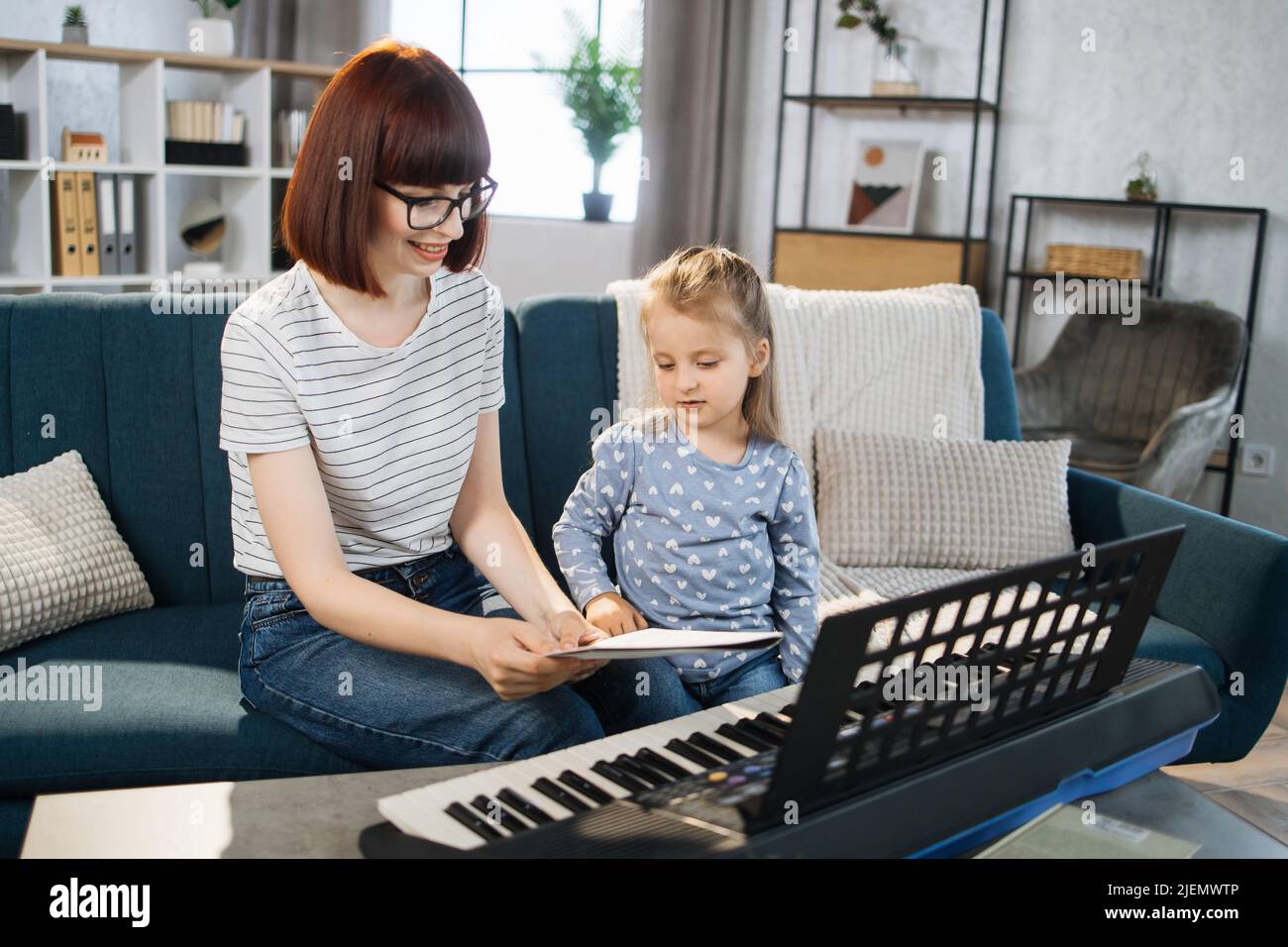 Child girl learning to play piano using notes together with her mother ...