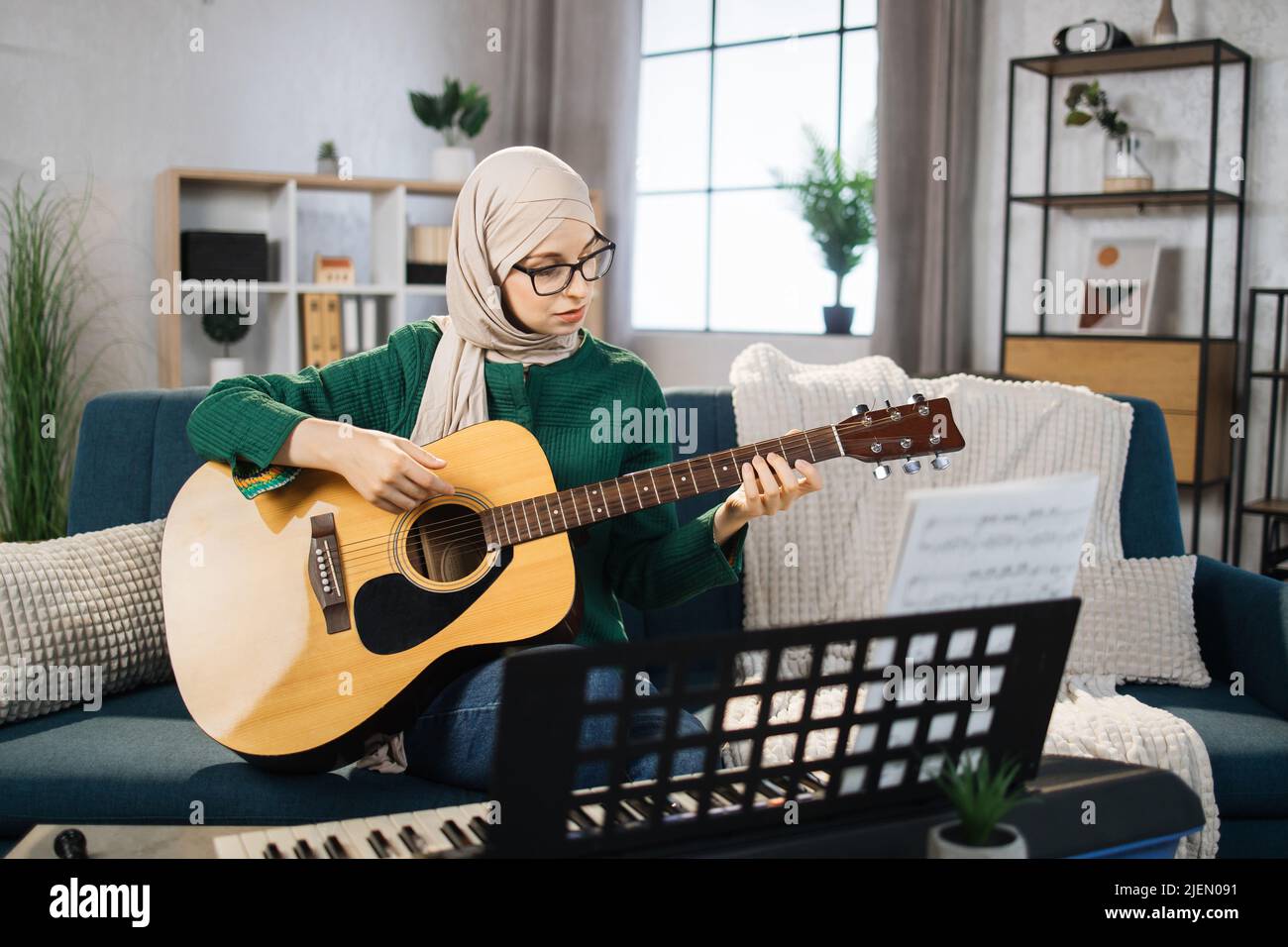 Young muslim woman in hijab plays guitar on bright living room at home ...