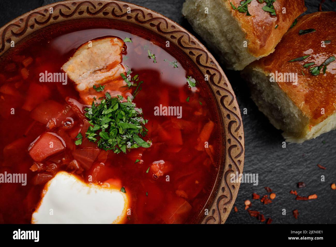 Red borscht with buns with garlic and sour cream, on a dark background ...
