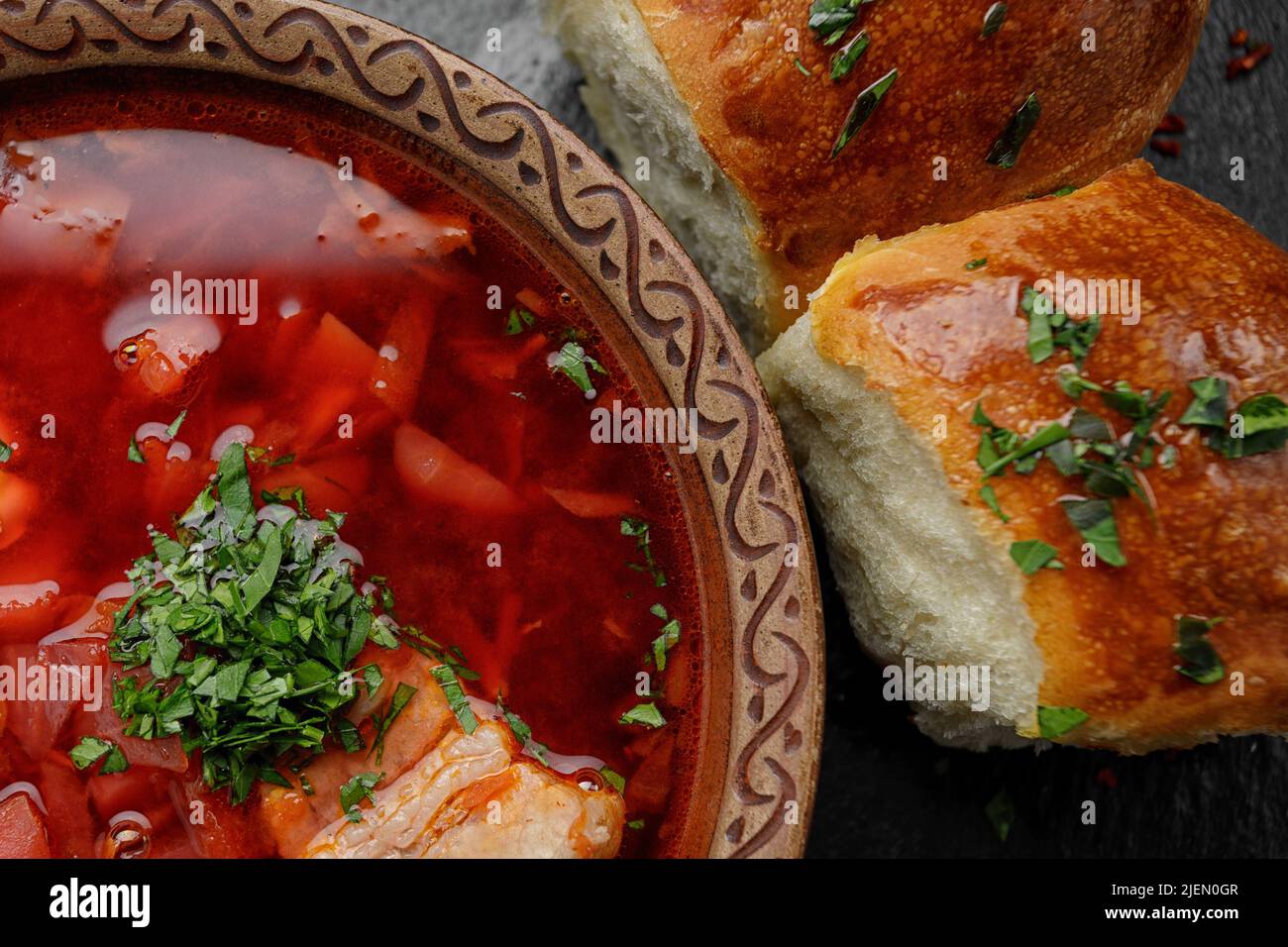 Red borscht with buns with garlic and sour cream, on a dark background ...