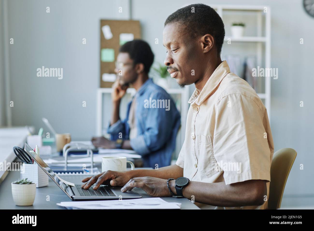 Side view portrait of adult black man using computer while working in office or coworking space ...