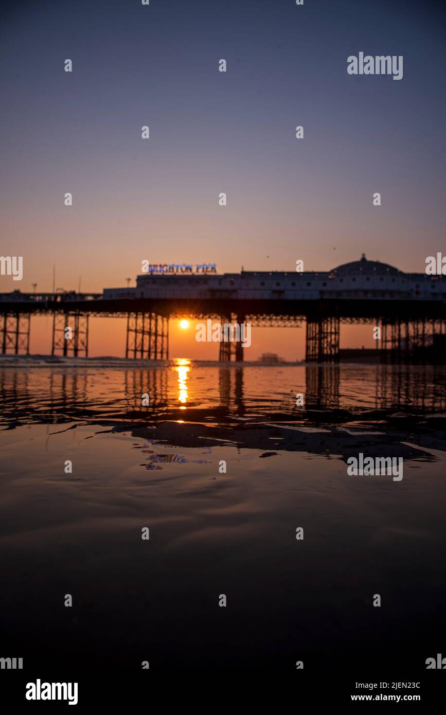 Sunset at Brighton Pier during low tide. West Pier is visible through ...