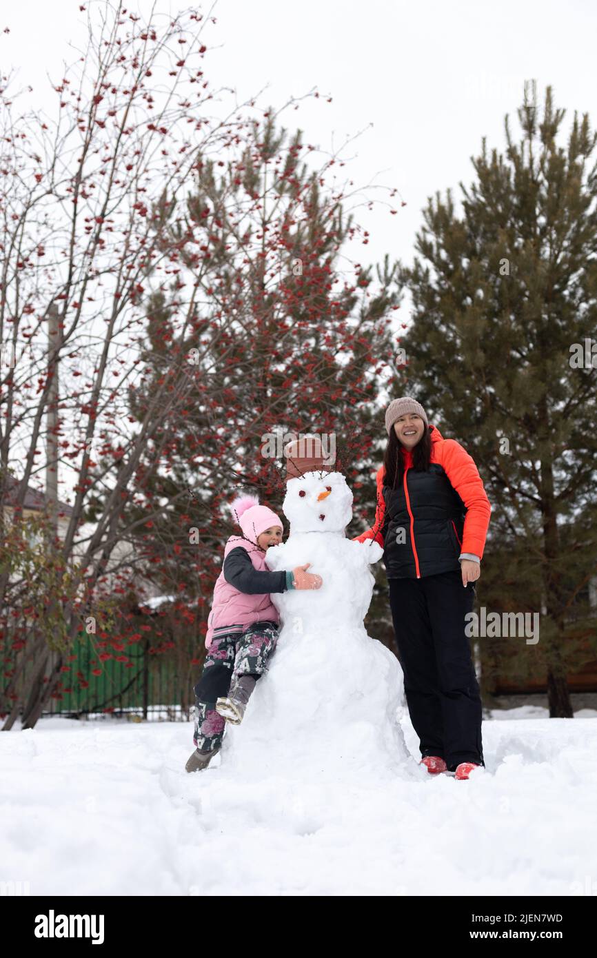 Low angle of smiling middle aged woman with daughter hugging snowman on ...