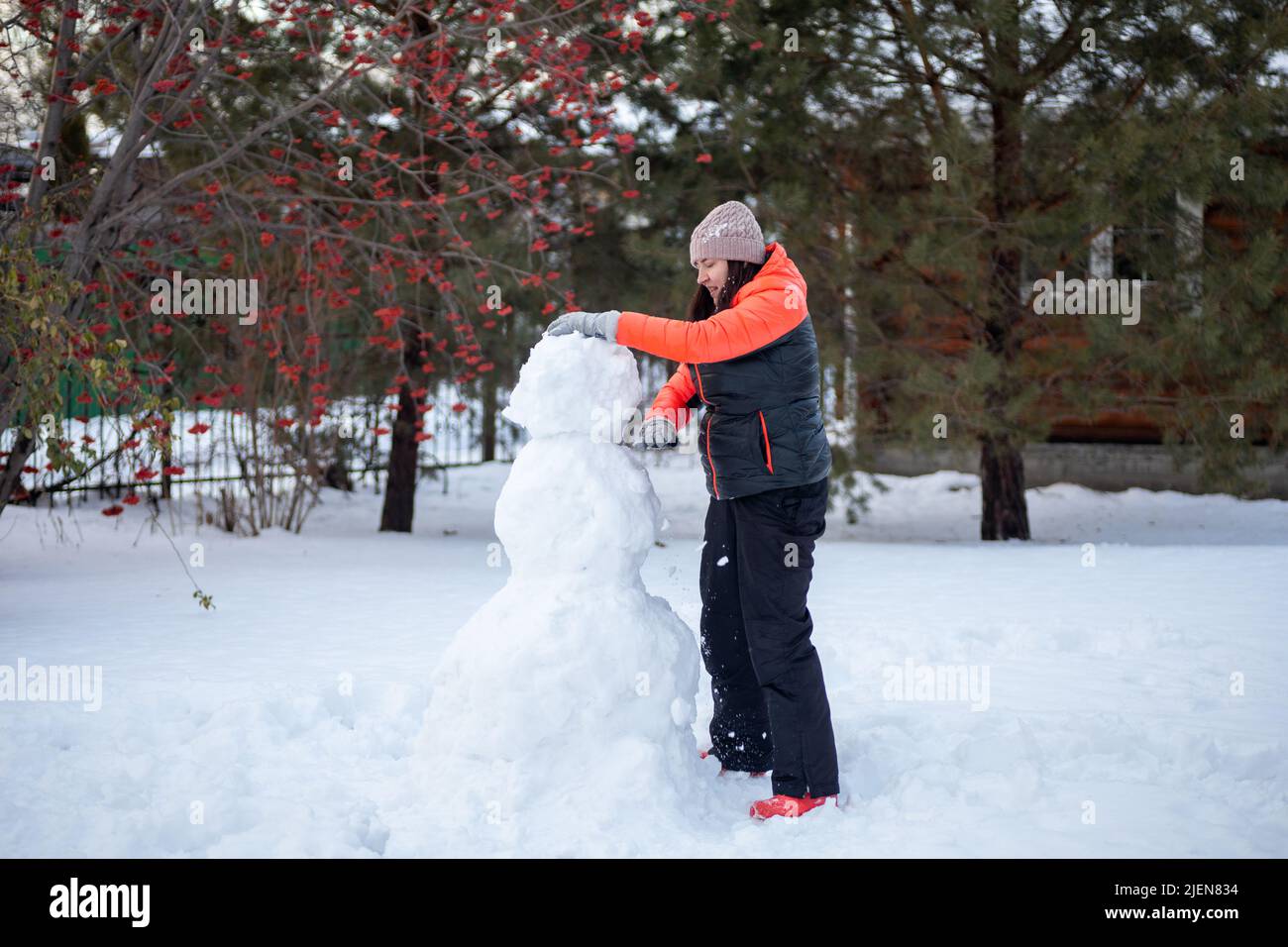 Female adult making snowman on her own on house backyard in evening ...