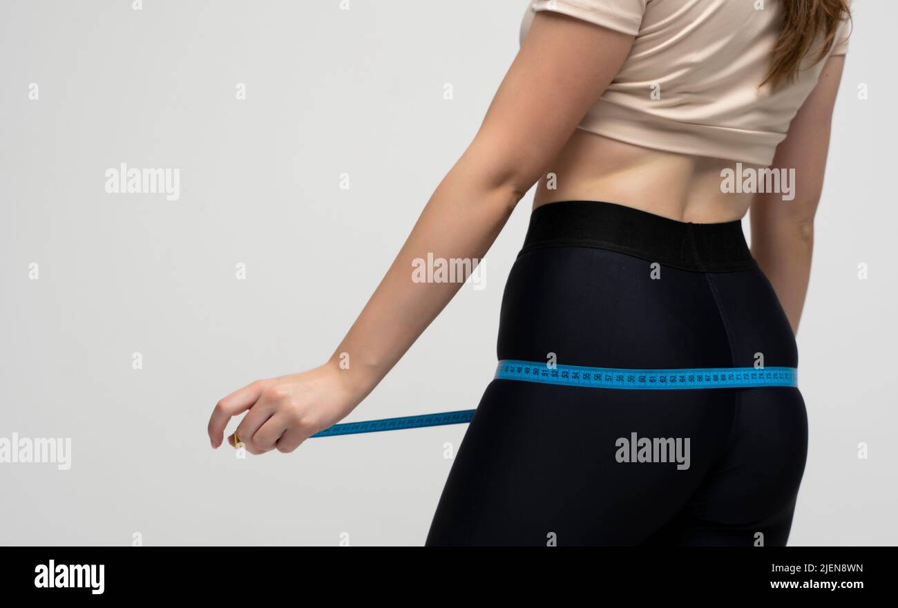 A slender girl measures her waist and hips with a centimeter on a white ...