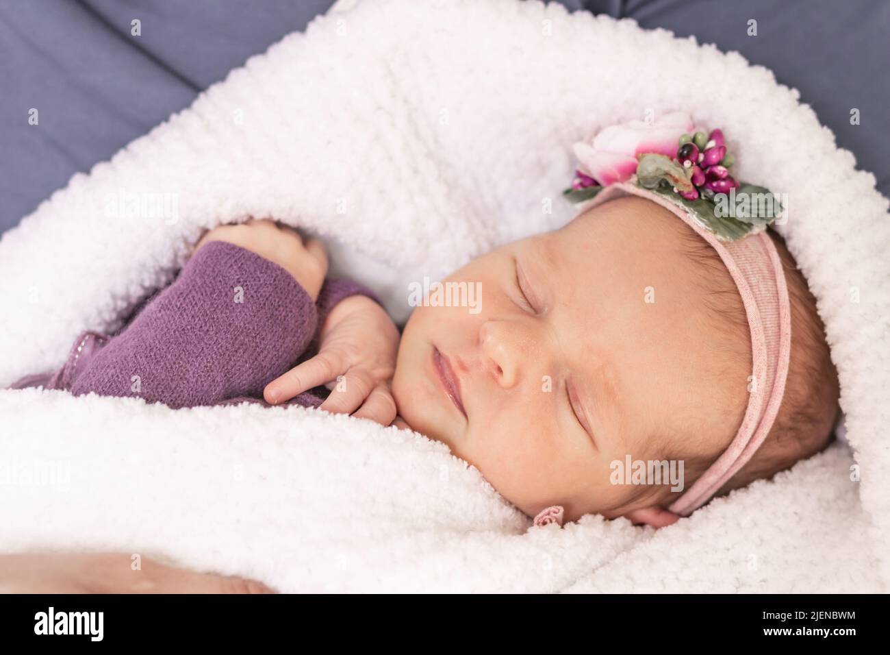 Sleeping newborn baby girl wrapped in a white fluffy blanket in the ...
