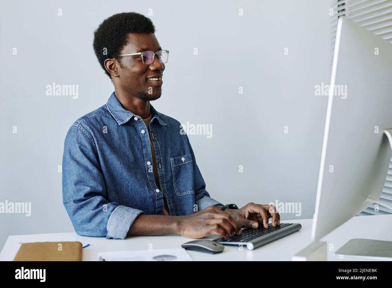 Minimal portrait of smiling black man using PC at workplace in office ...