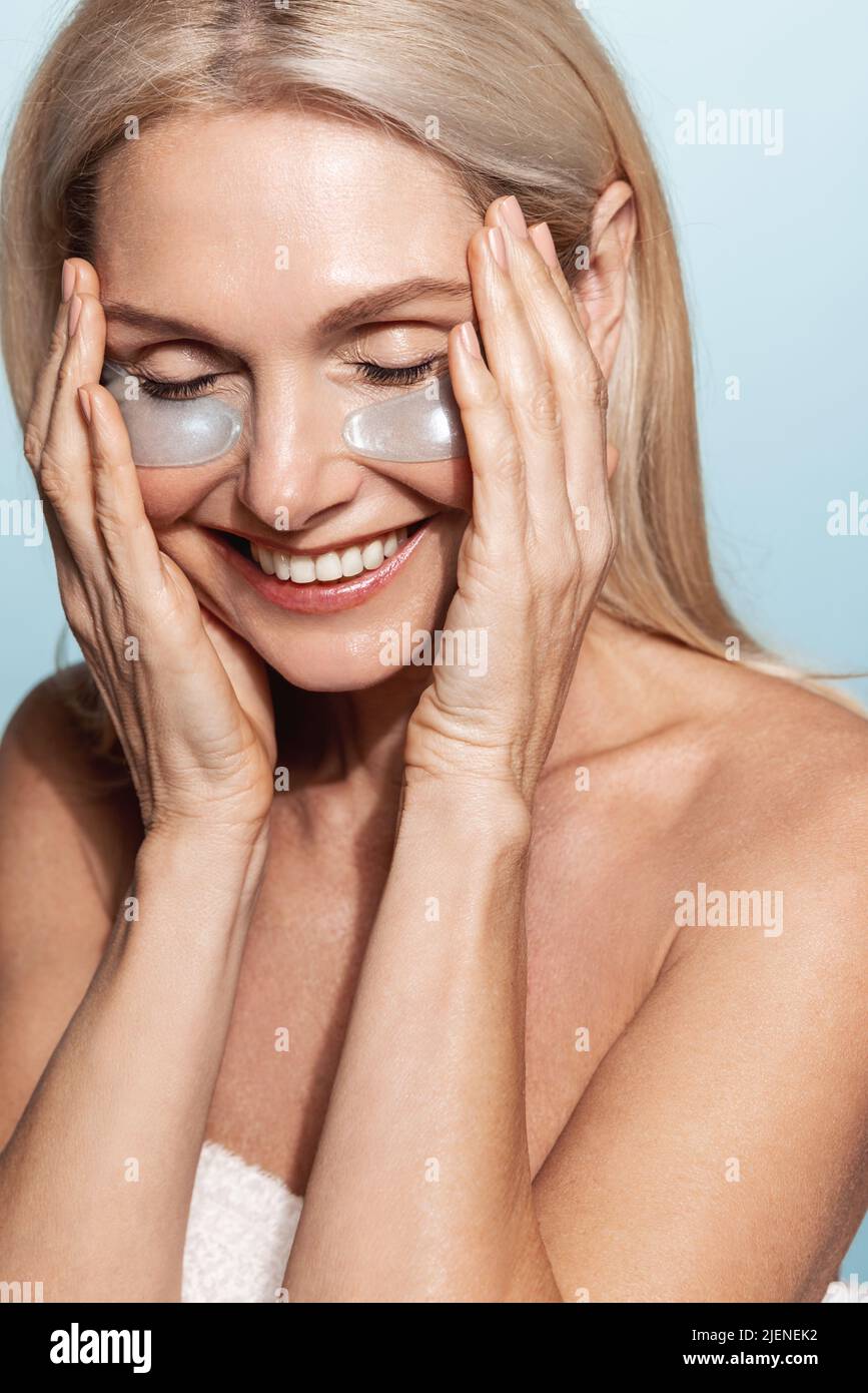 Rejuvenation and skincare. Beautiful smiling lady, 50 years old, using ...
