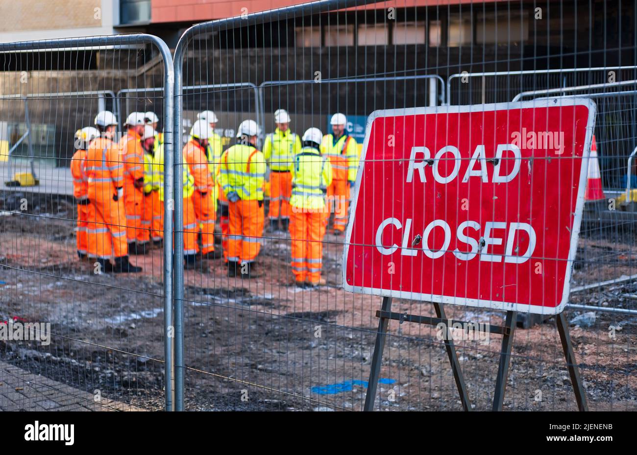 Red Road Closed sign with construction workers gathered for instruction ...
