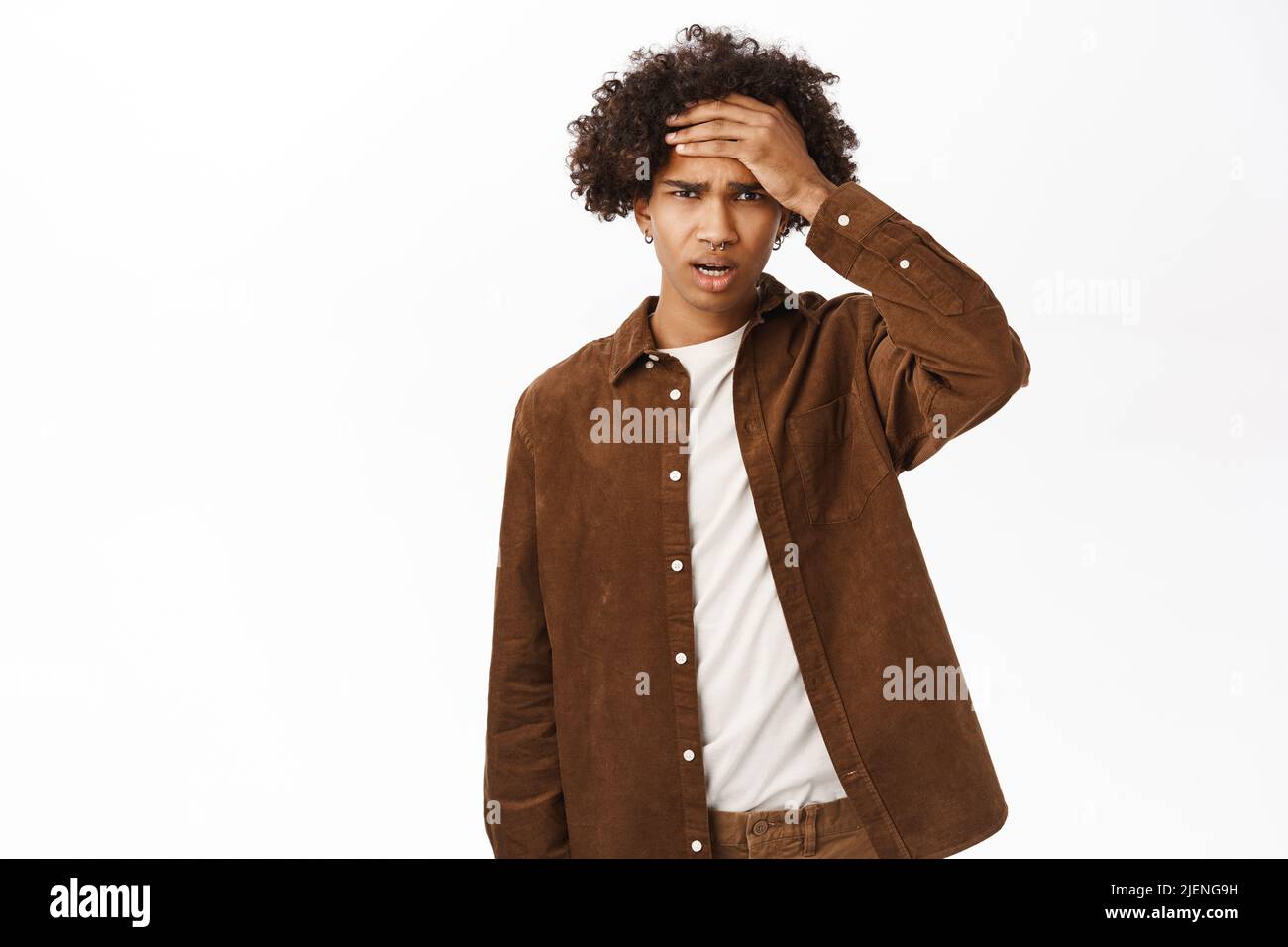 Troubled young hispanic man holds hand on head, looks worried and ...