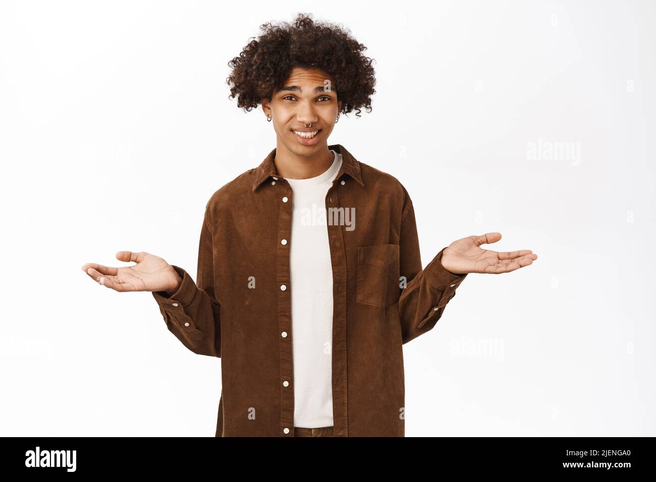 Clueless young hispanic man shrugs shoulders, smiles nervously, saying ...