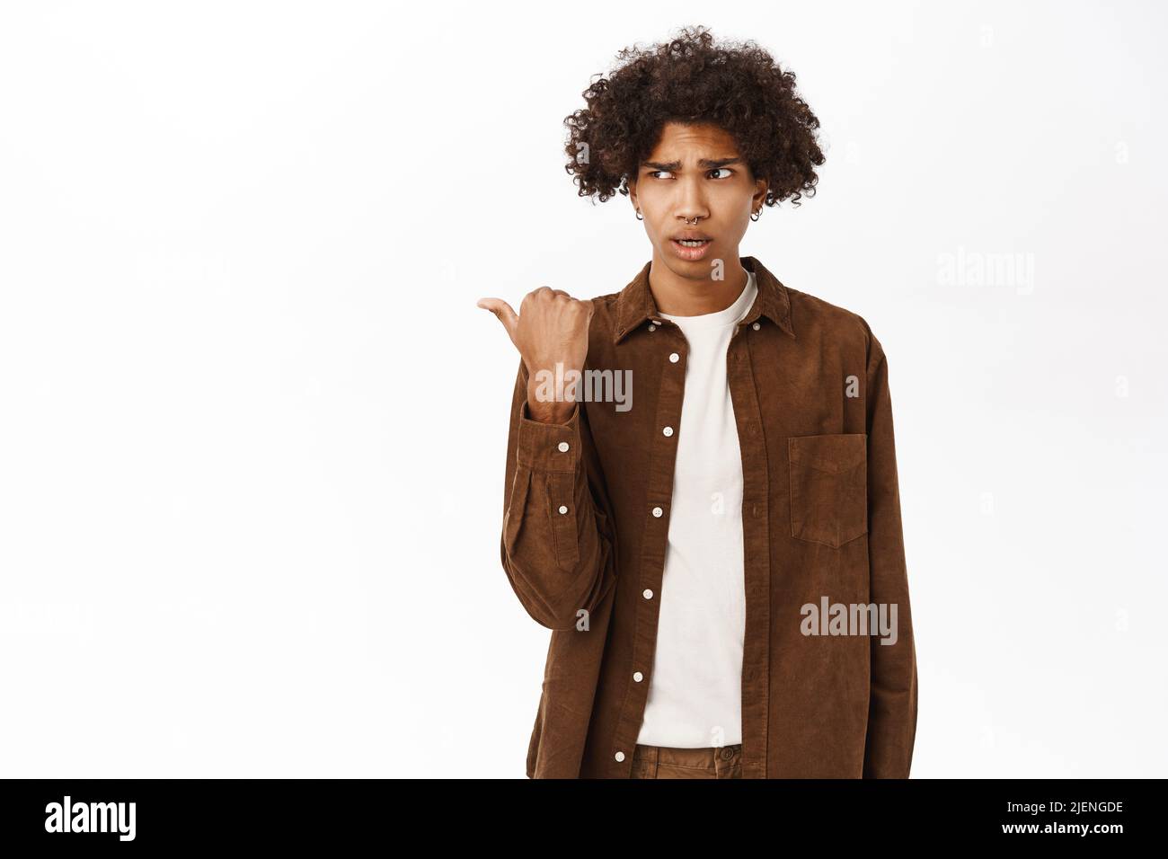 Portrait of confused young man pointing finger left, looking puzzled at ...