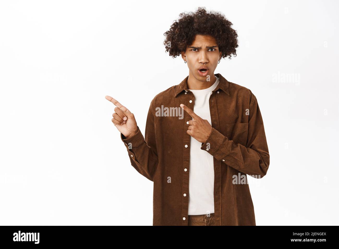 Shocked and concerned young man pointing fingers left, looking at you ...