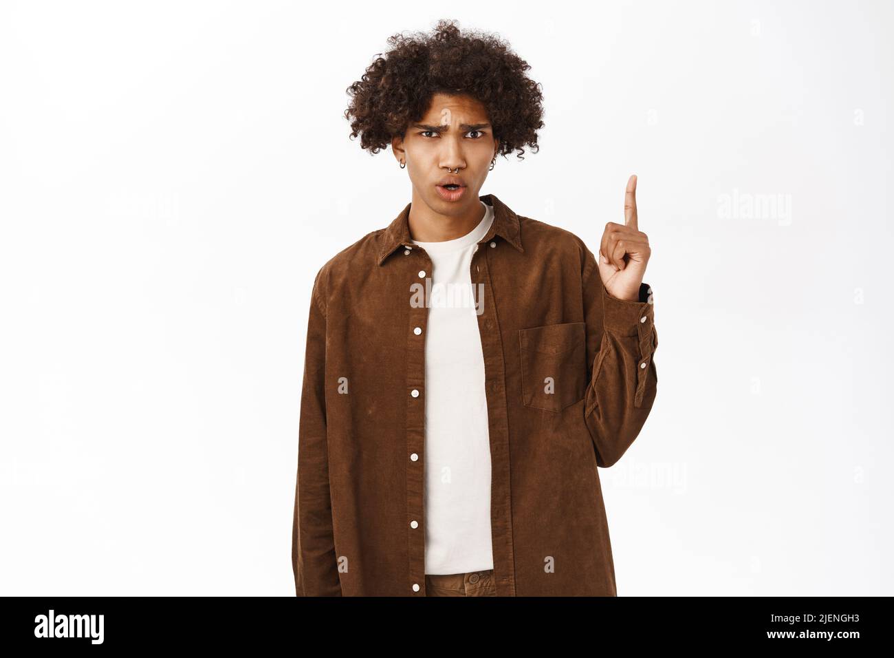 Confused young man, 18 years, pointing finger up, look at smth unfair ...