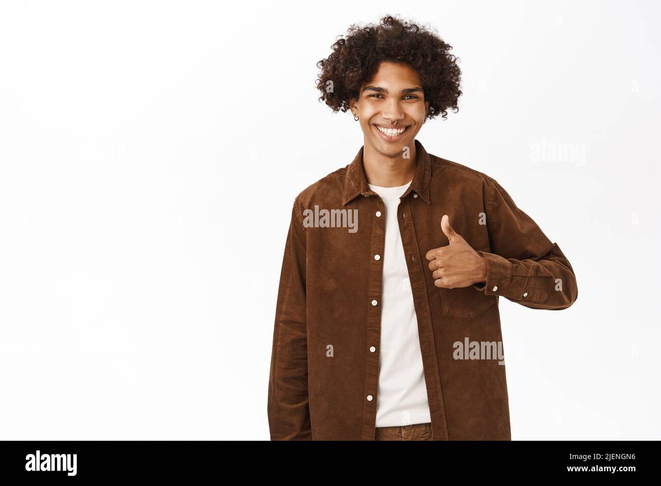 Handsome boy shows thumbs up and smiles pleased, stands over white ...