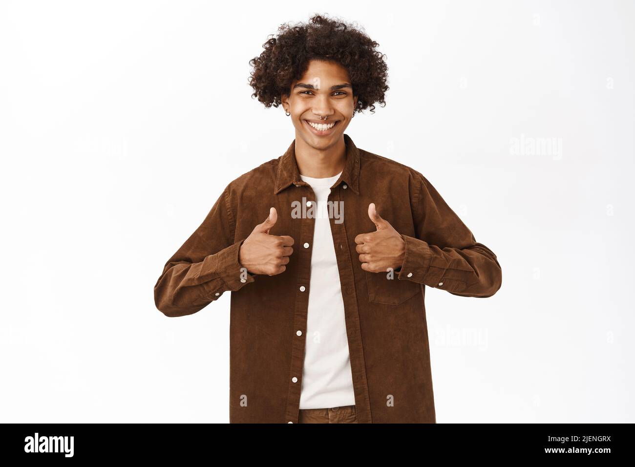 Handsome smiling young man shows thumbs up in support, pleased by smth ...