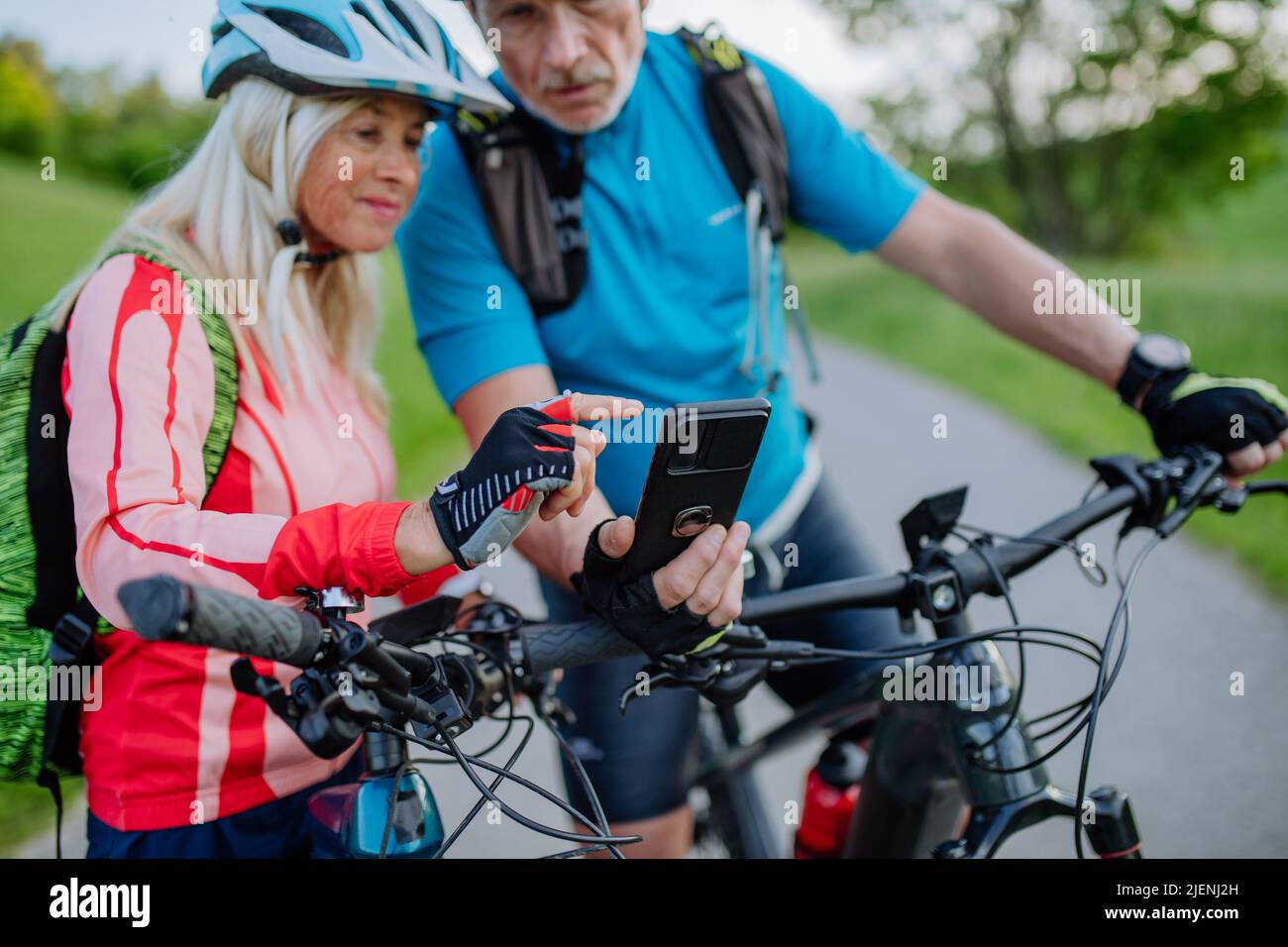Active senior couple resting after bicycle ride at summer park, using ...