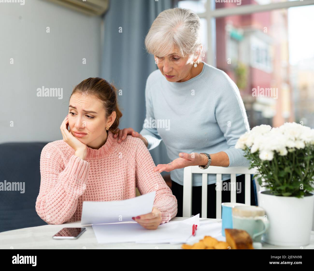 Upset young woman with aged mother looking worriedly at papers at home ...