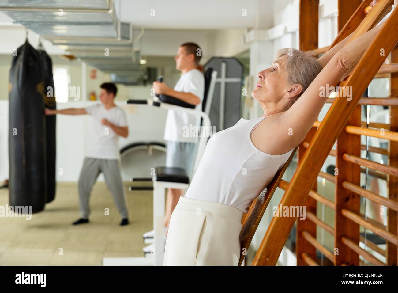 Mature woman doing stretching of body and legs on special simulator in ...