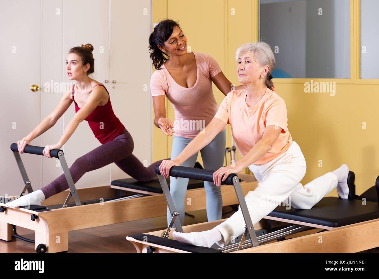 Pilates instructor assisting elderly woman to do exercises on reformer ...