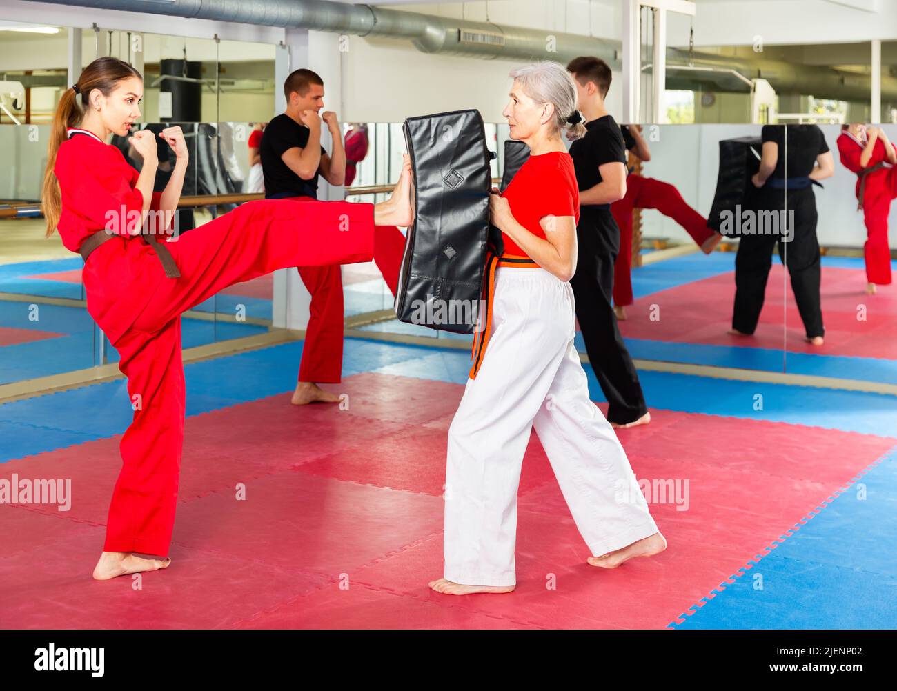 Woman exercising kicks on punching pad during group karate training ...