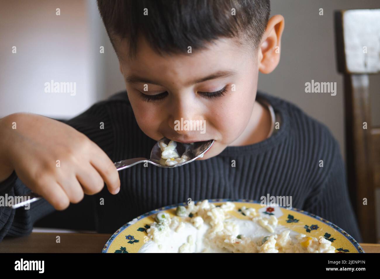Close-up portrait of caucasian little boy eating porridge with spoon in ...