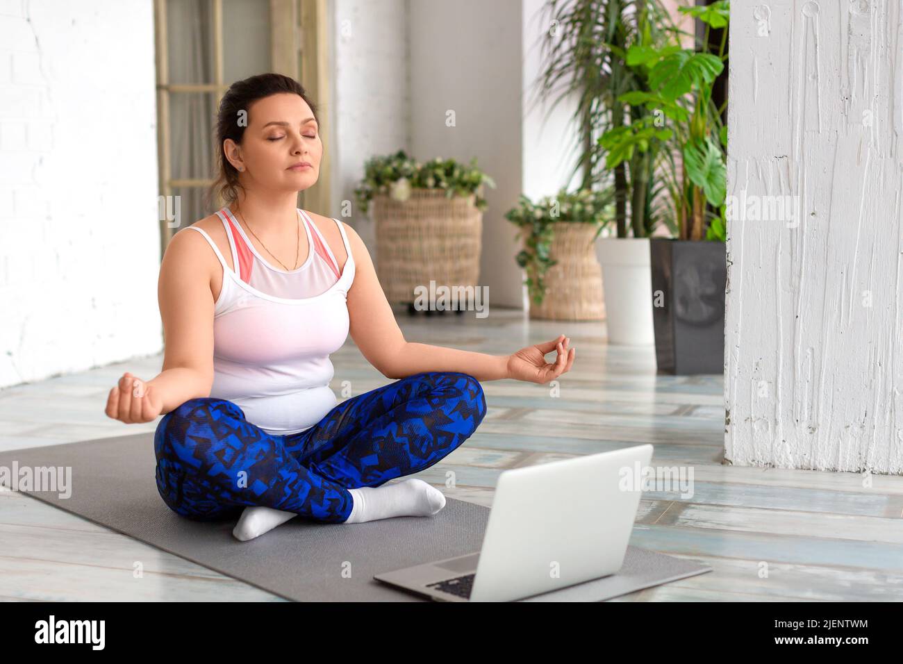 Woman meditate with close eyes in front of laptop in home interior ...
