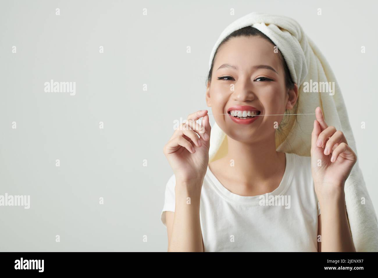 Young woman gently sliding floss between gum and teeth after shower ...