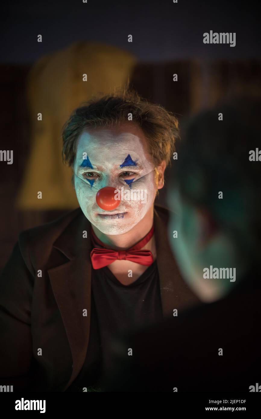 Clown concept - a man with cracked clown painted face looking in the ...