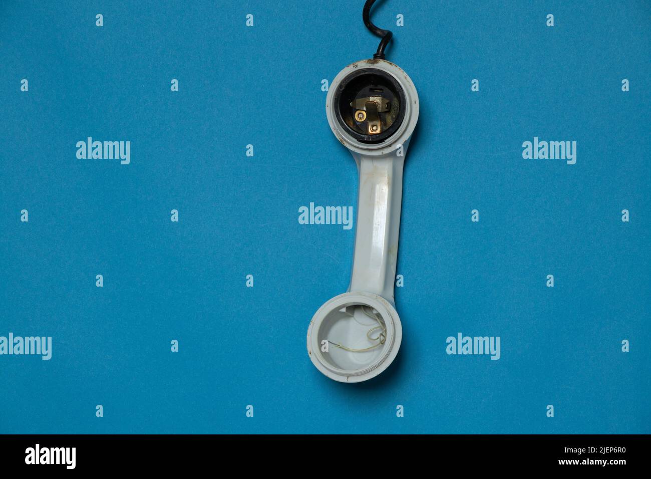 old broken telephone receiver on wire weighs on blue isolated ...