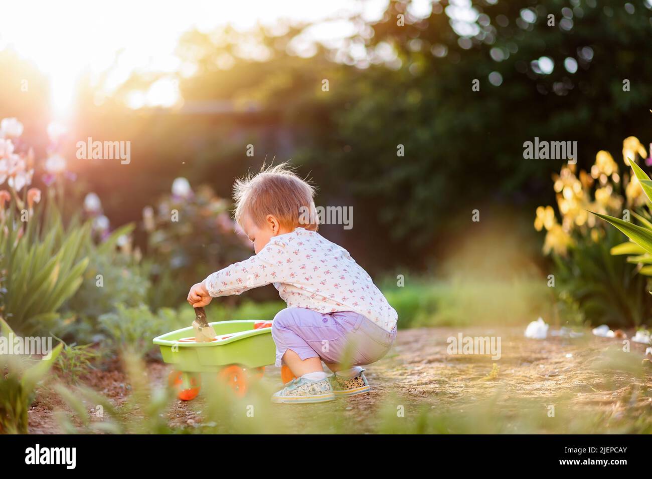 Cute baby playing with a plastic toy cart at the garden. Baby sits and ...