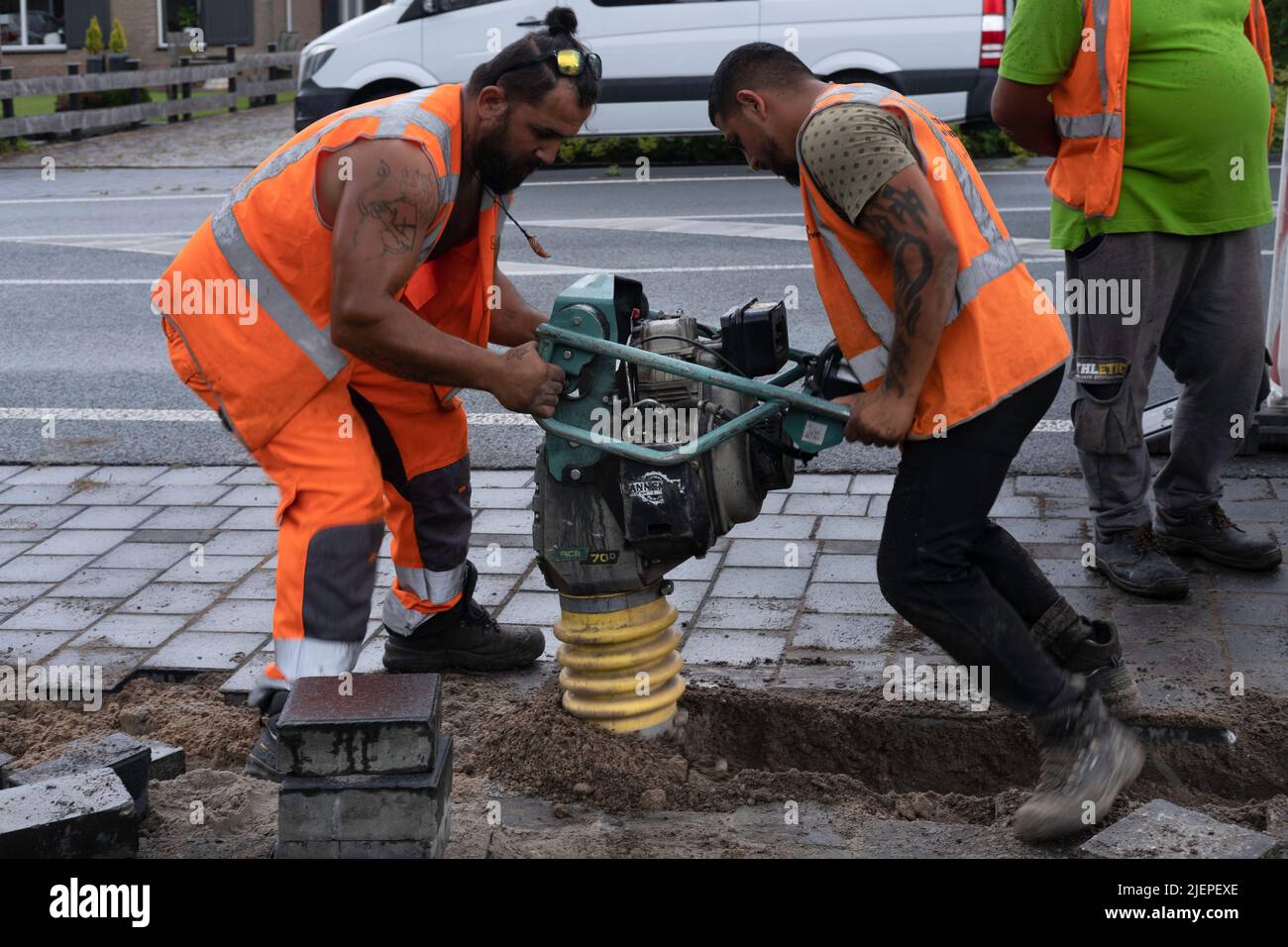 Two workers wield a portable vibration rammer to tamp down the sand ...