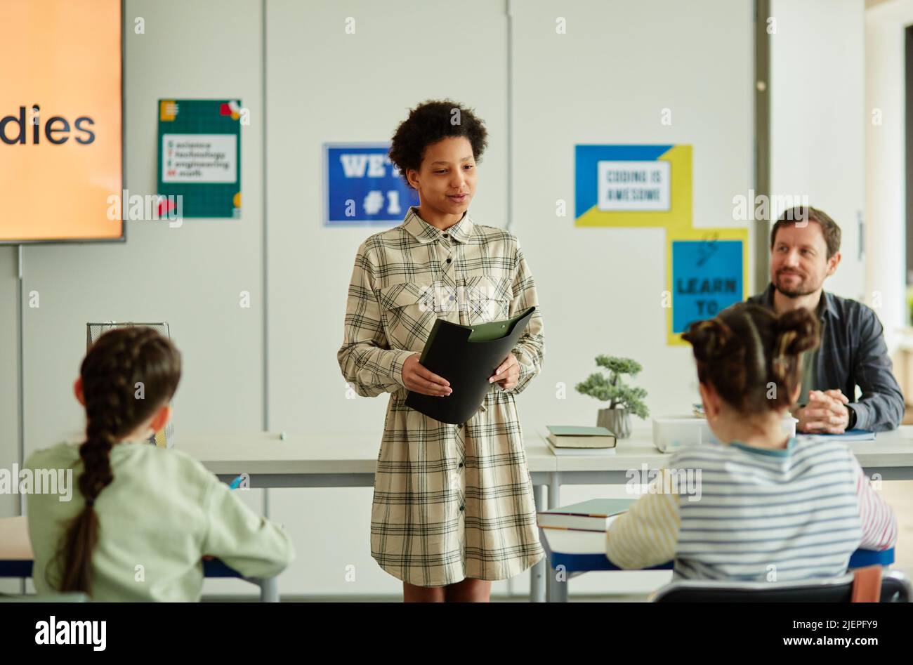 Portrait of young black girl giving presentation in school to group of ...