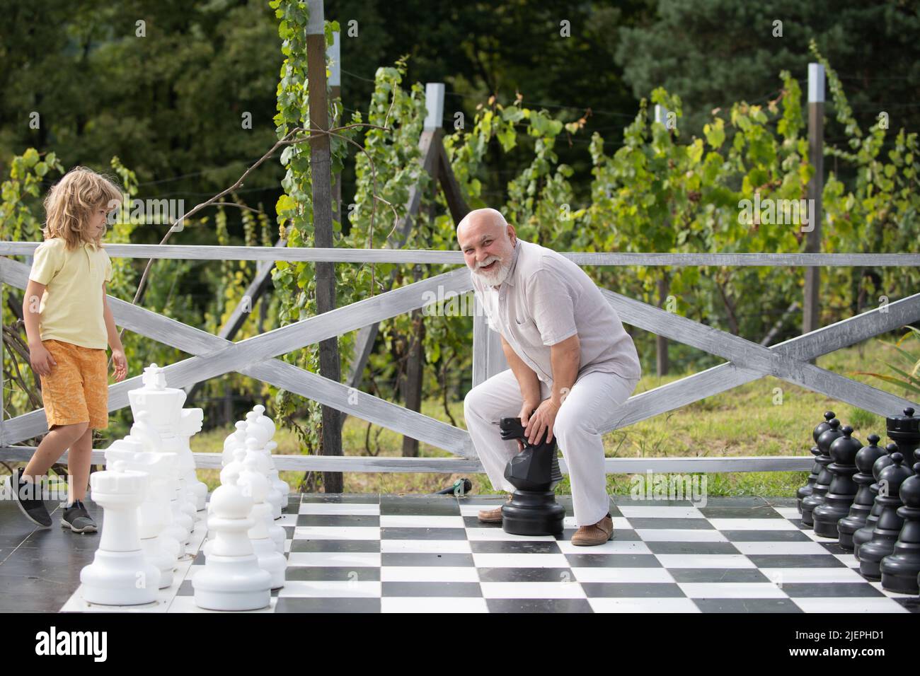 Grandfather and grandson playing chess on big chess board. Generations ...