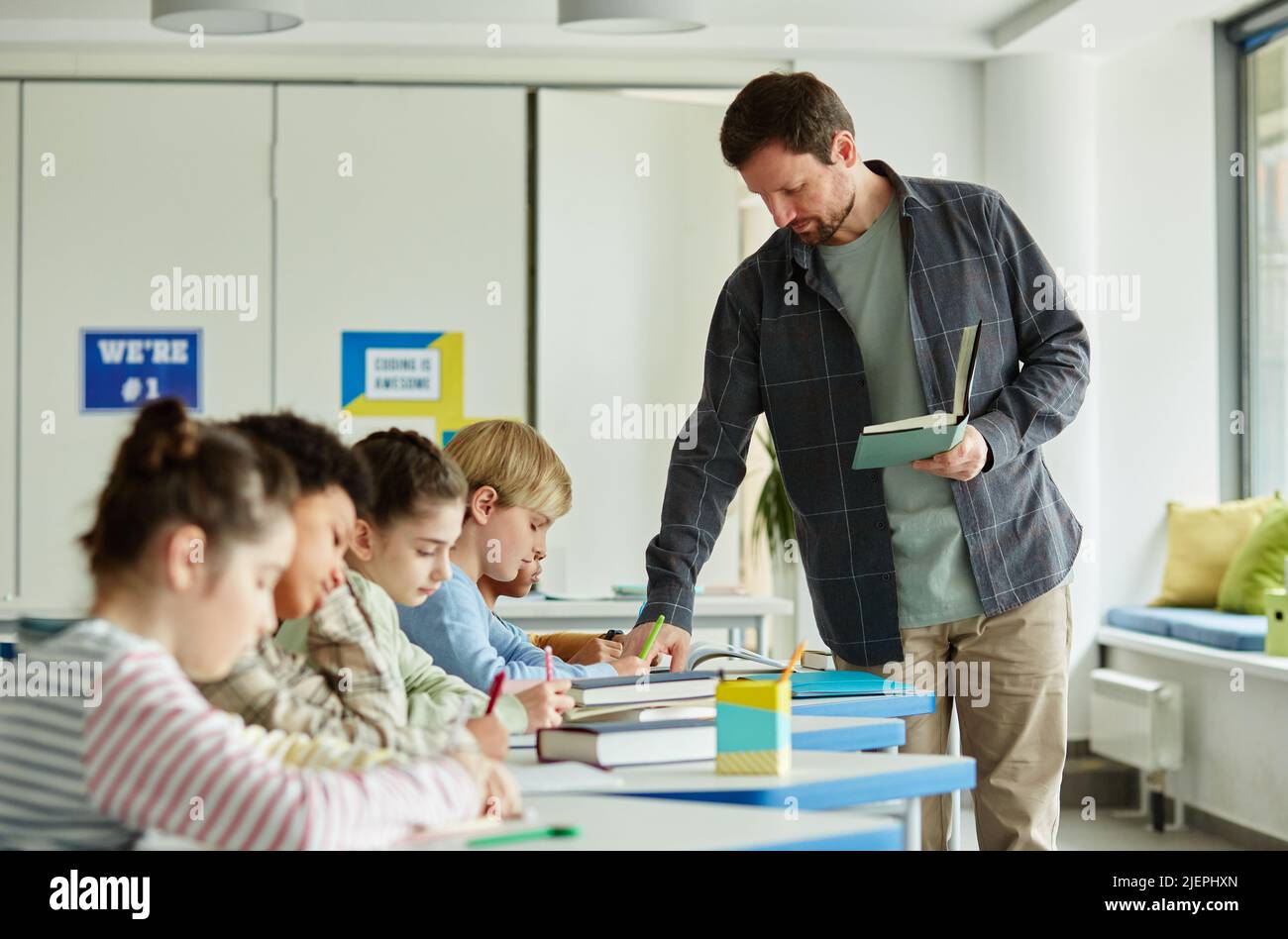 Side view portrait of male teacher helping children taking test in ...