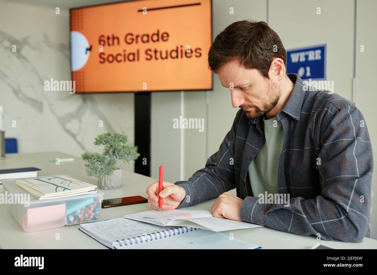 Portrait of male teacher sitting at desk in school classroom and ...