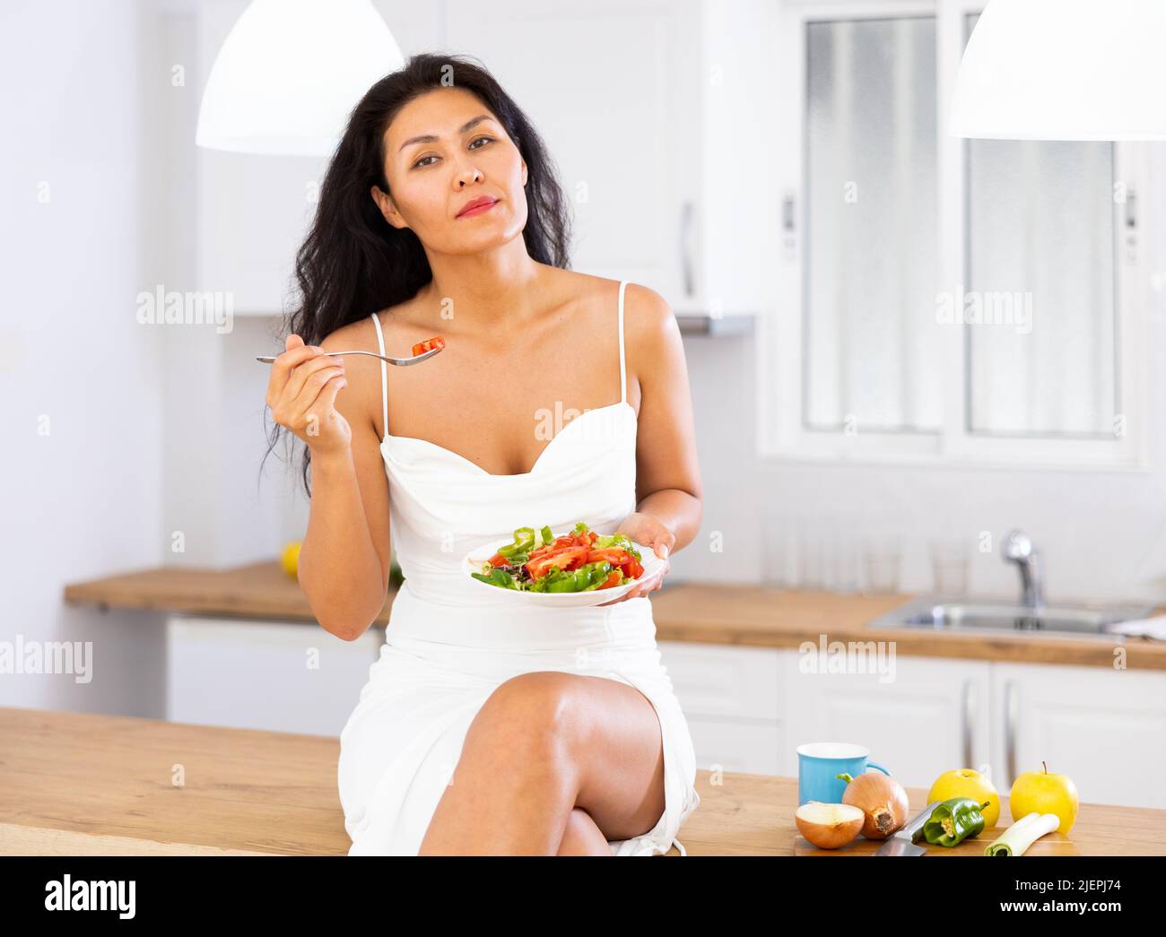 Woman sitting on kitchen table and eating salad Stock Photo - Alamy