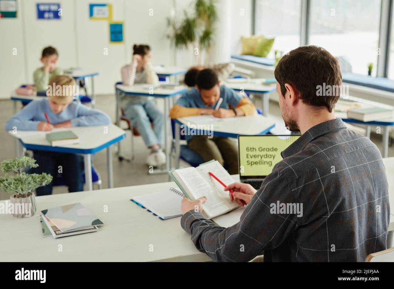 Back view at male teacher sitting at desk in classroom with group of ...