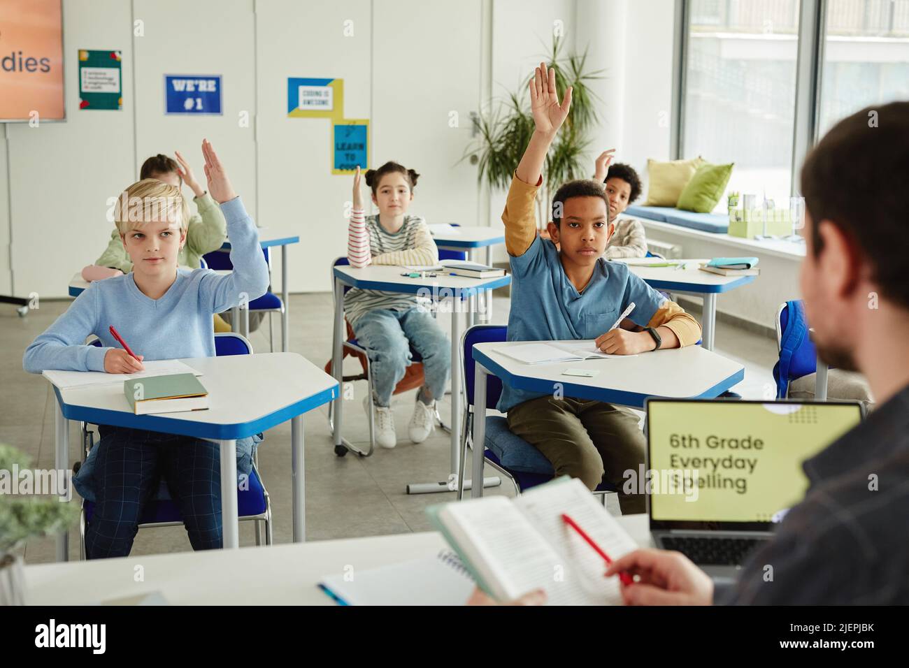 Diverse group of children raising hands in class and answering ...