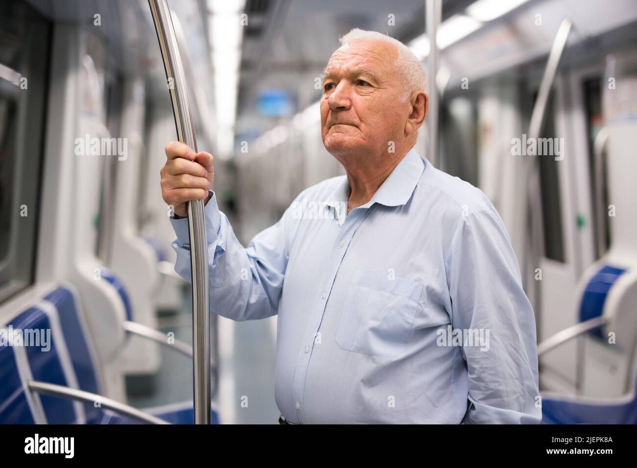Elderly caucasian man standing in subway car and holding handrail while ...