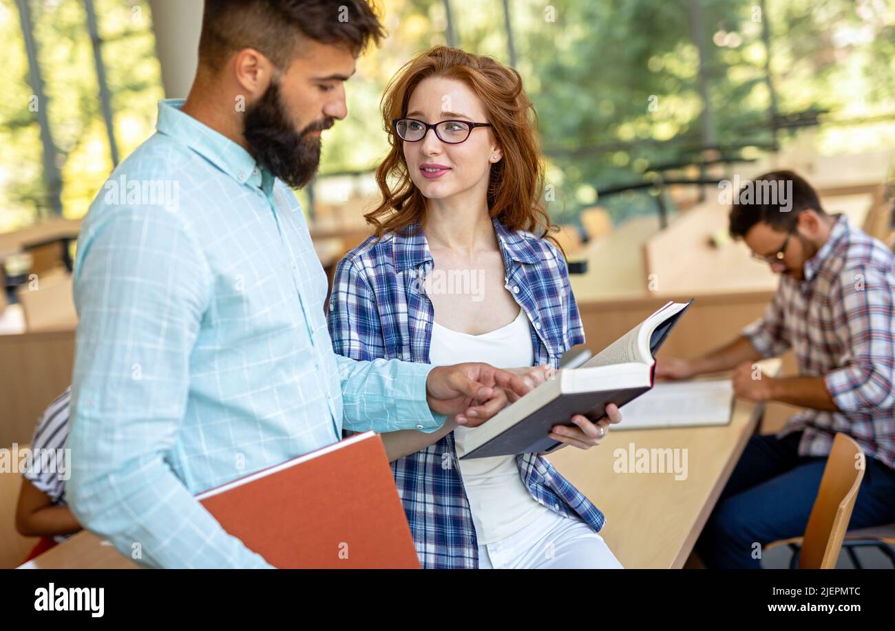 Happy university students studying with books in library. Group of ...