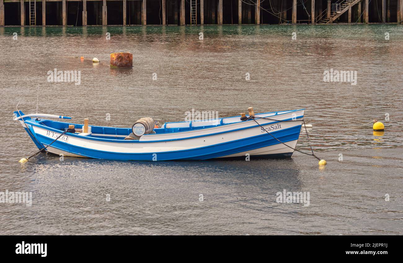 A rowing boat with barrels is moored to buoys in harbour. A quayside is ...