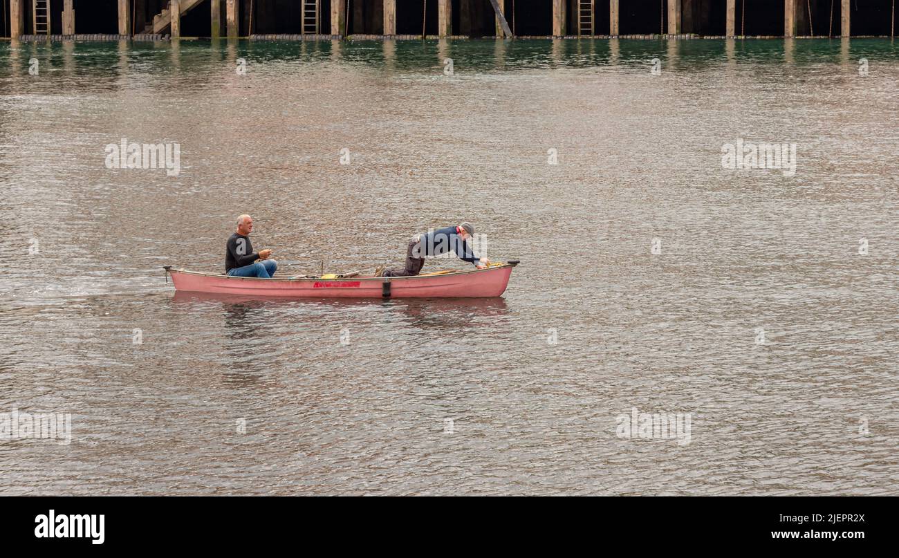 Two men in a rowing boat; one is paddling the other is leaning forward ...